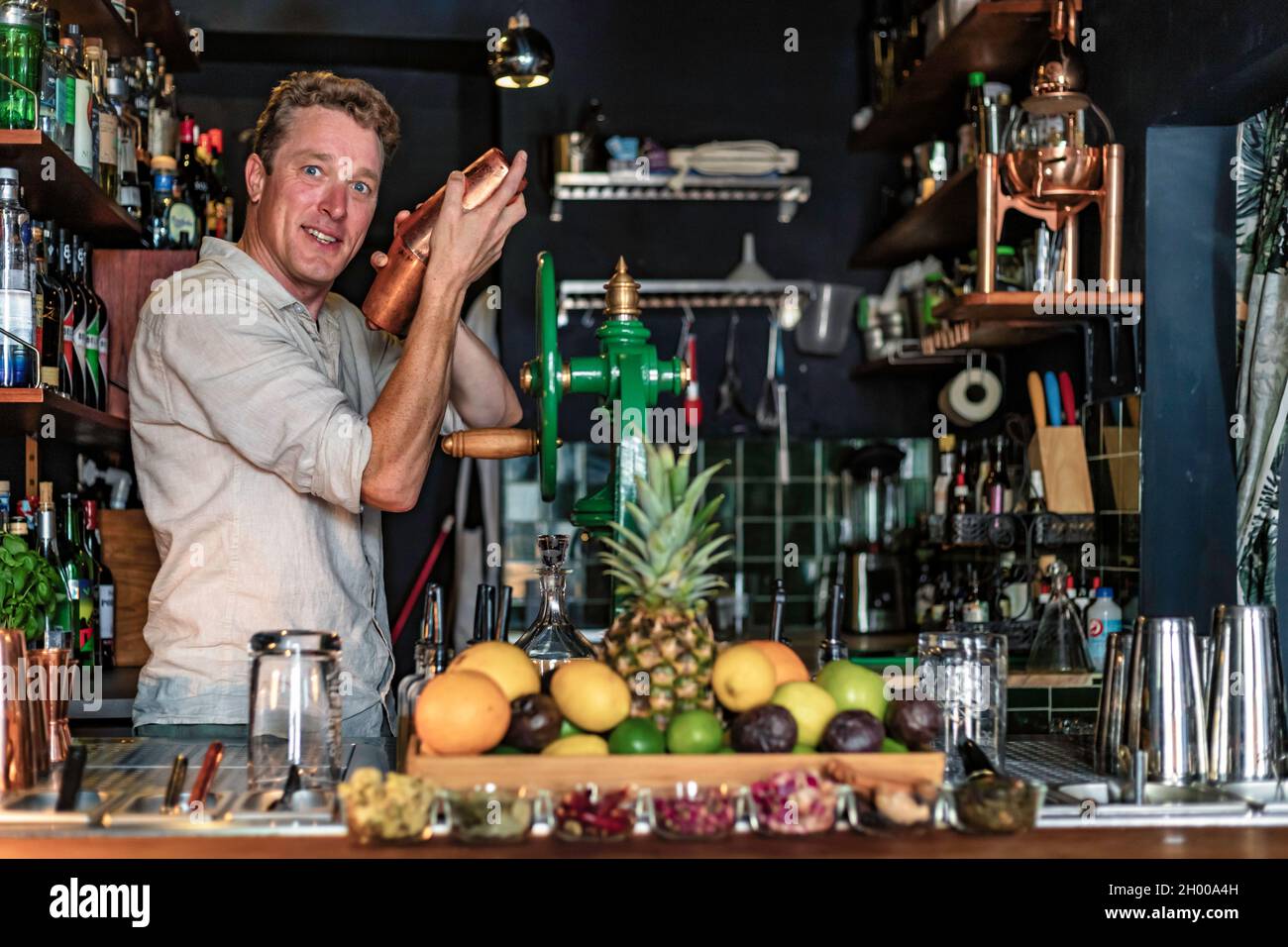 View of a cheerful man working as bartender in a colourful cocktail bar ...