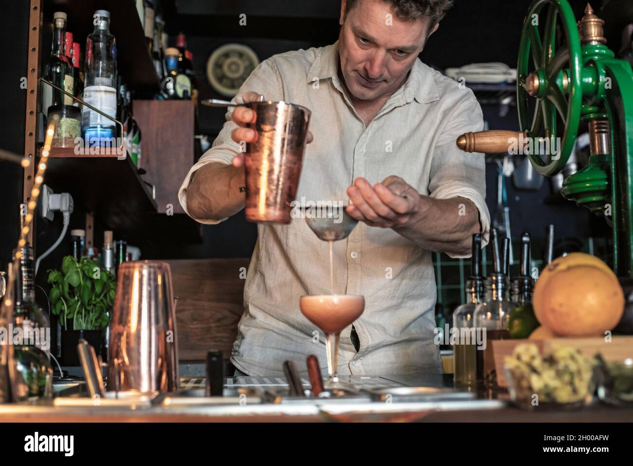 Expert bartender pouring a cocktail in a glass from the shaker in his ...