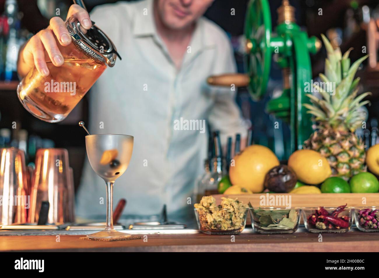 A professional bartender pouring a cocktail in a glass from a shaker ...