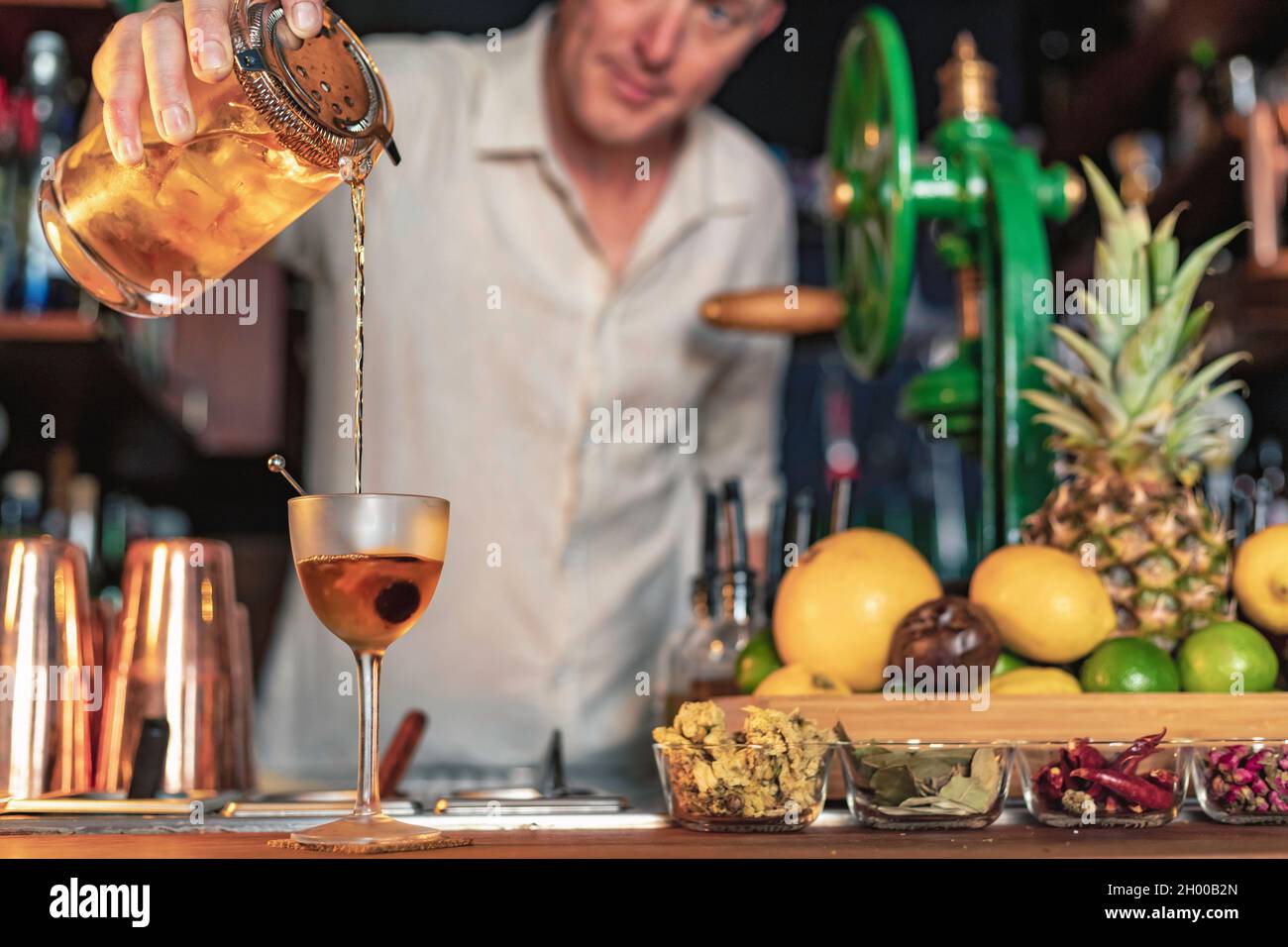 A professional bartender pouring a cocktail in a glass from a shaker ...