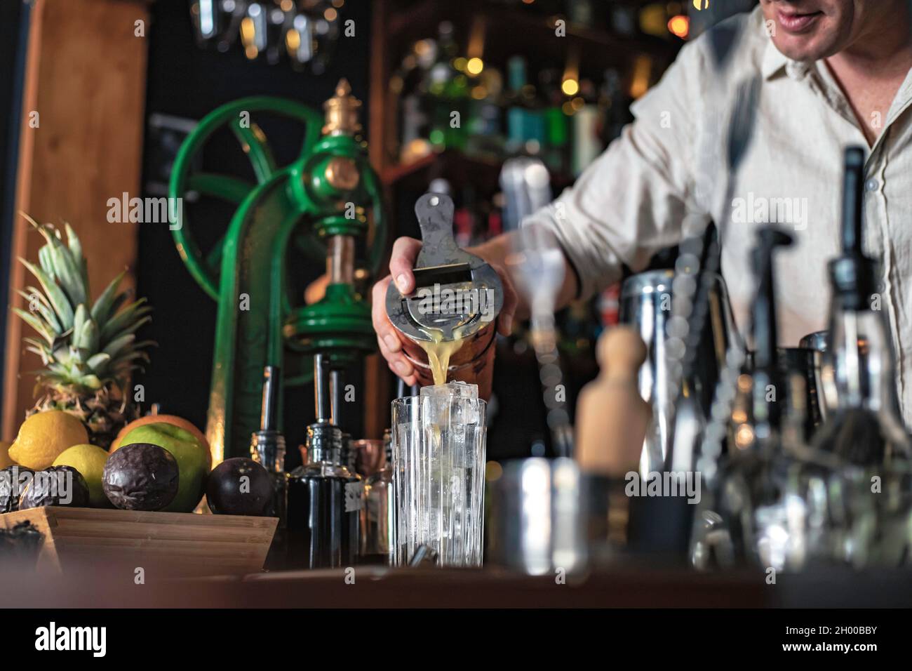 A professional bartender pouring a cocktail in a glass from a shaker ...