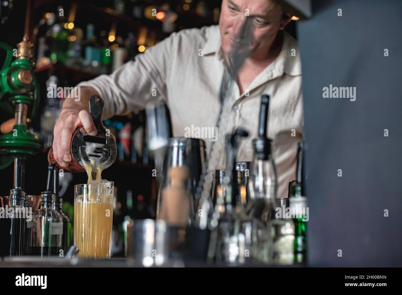 A professional bartender pouring a cocktail in a glass from a shaker ...