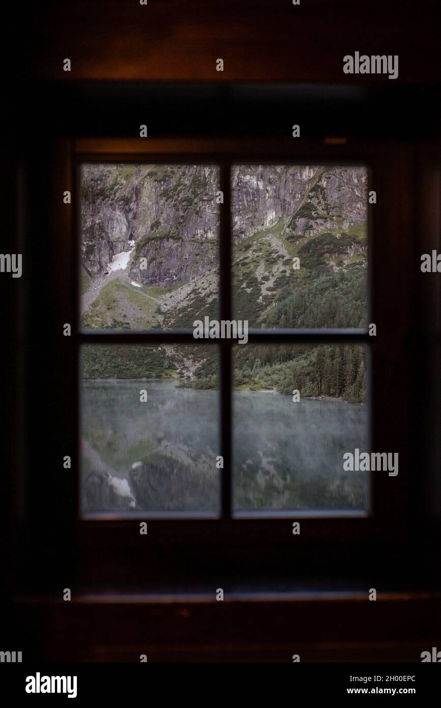 A vertical view of mossy rocks by the lake behind a window with wooden ...
