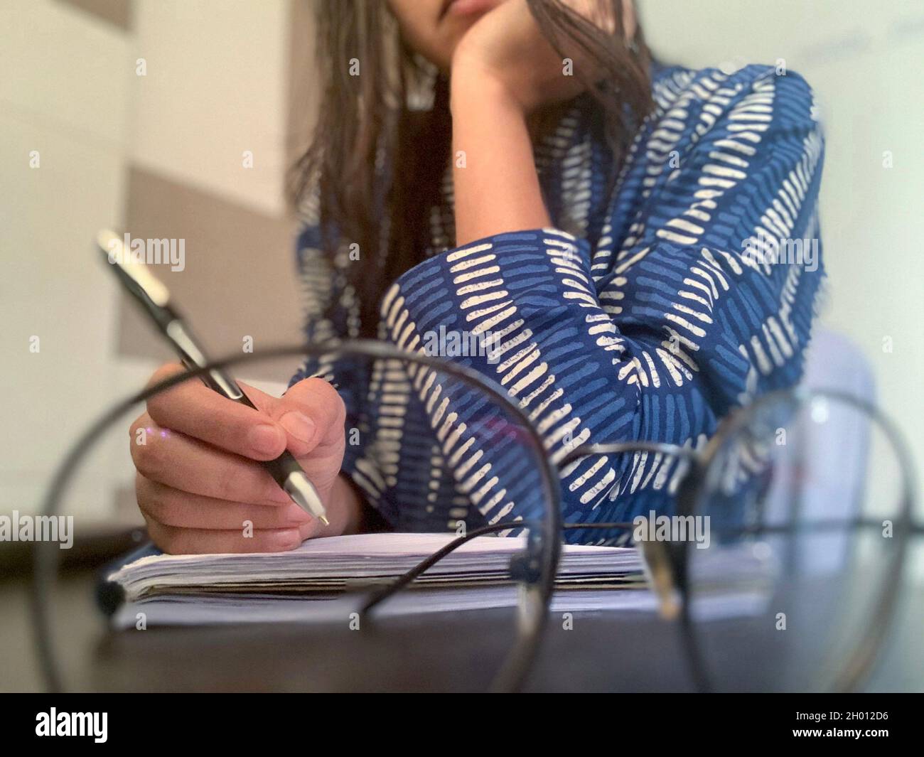 A girl in deep thought writing on a notepad. India Stock Photo - Alamy