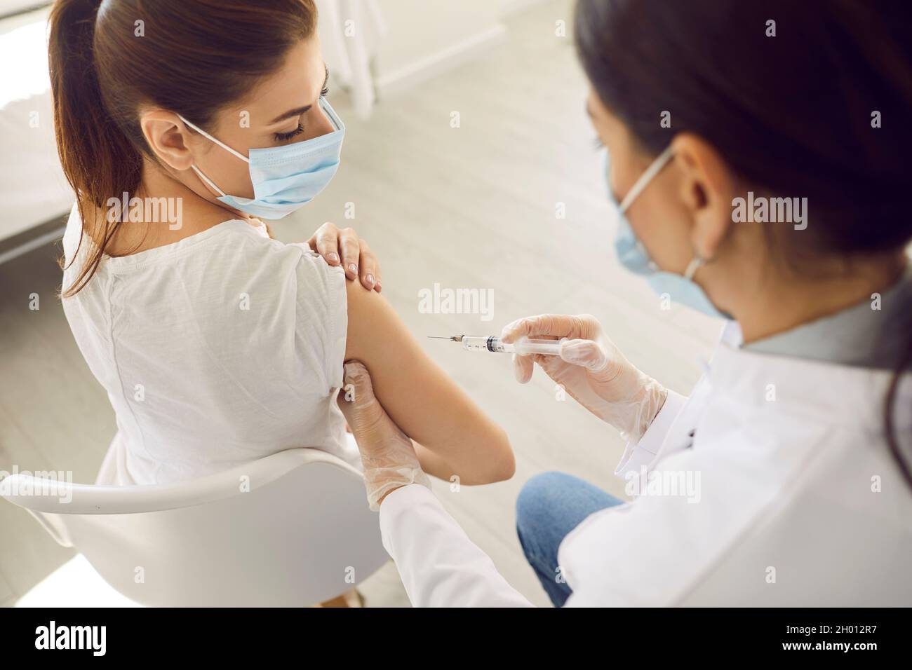Young woman wearing a medical face mask is getting a vaccine injection ...