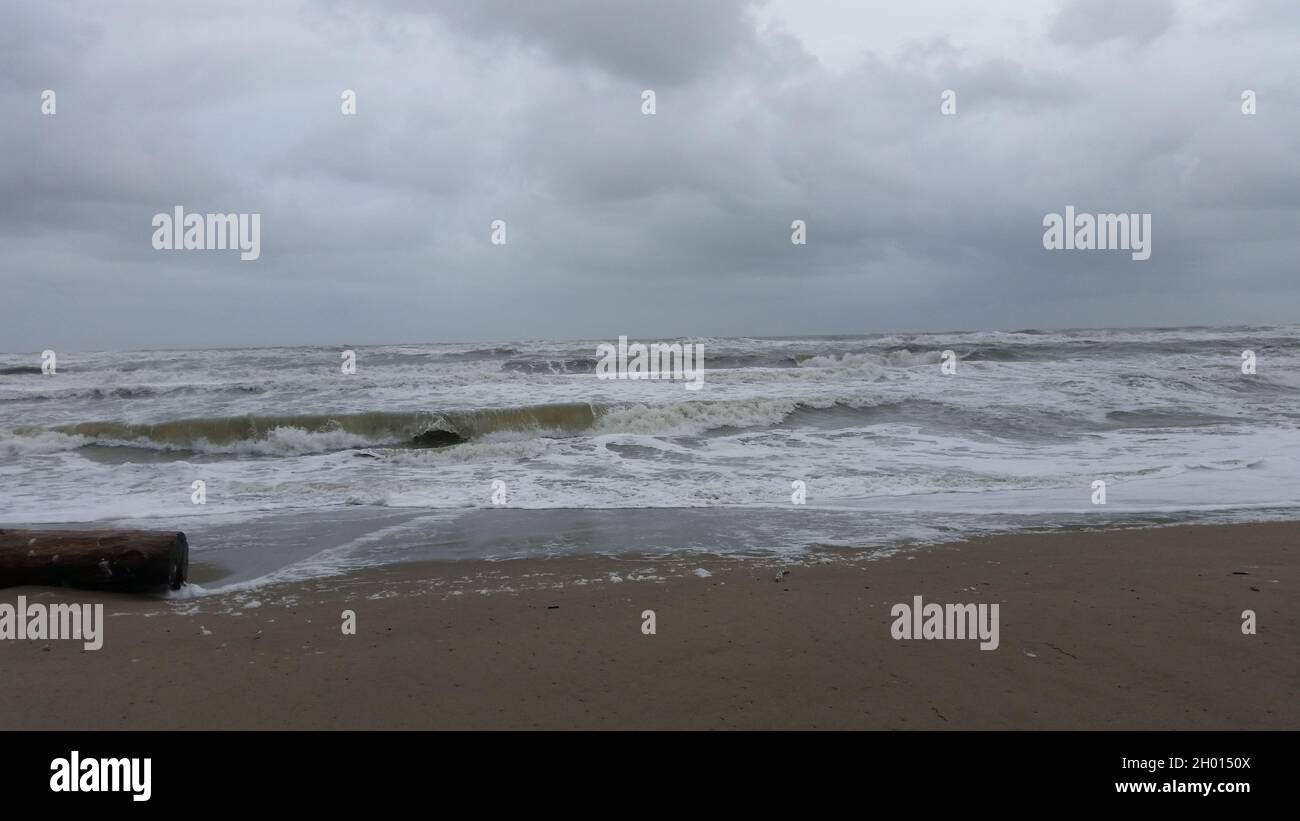 A foamy ocean waves breaking on a sandy beach under a dark cloudy sky ...