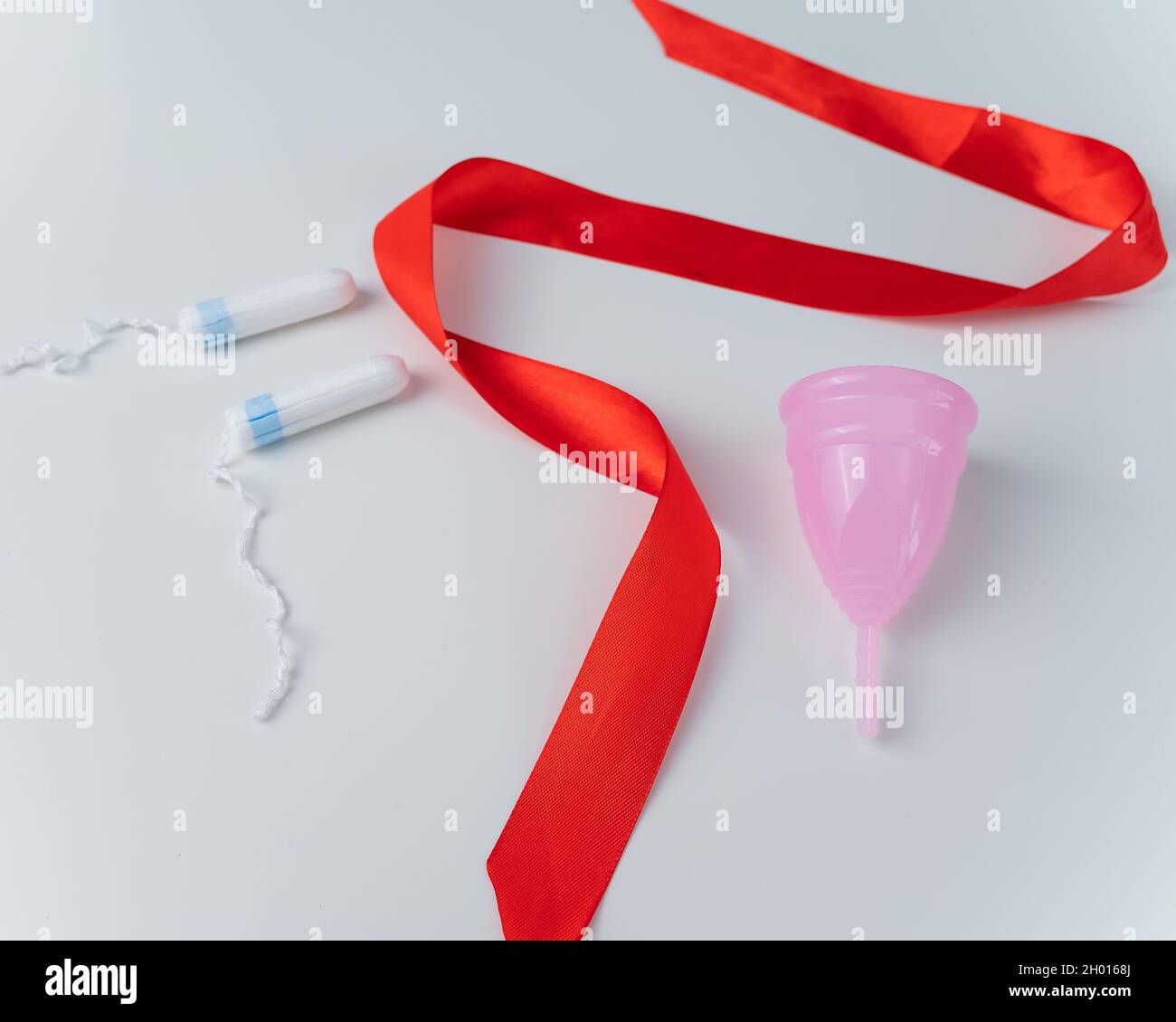 Tampon, pink menstrual cup and red satin ribbon on a white background ...