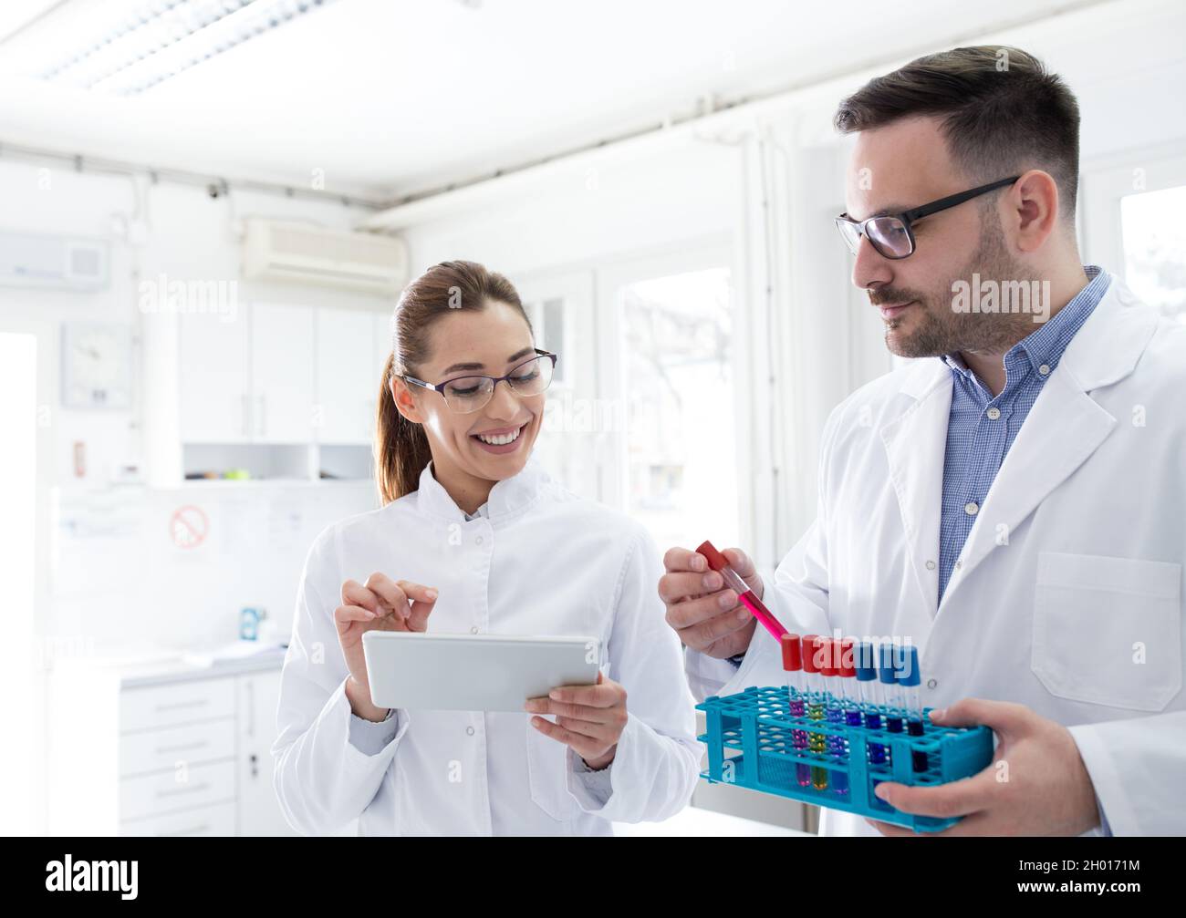 Two doctors checking samples in test tubes and looking at tablet in ...
