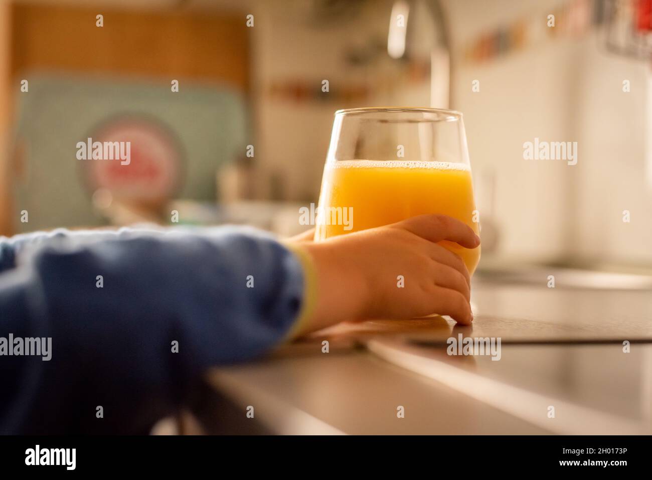 Child's hands grabbing a crystal glass with orange juice on the kitchen ...