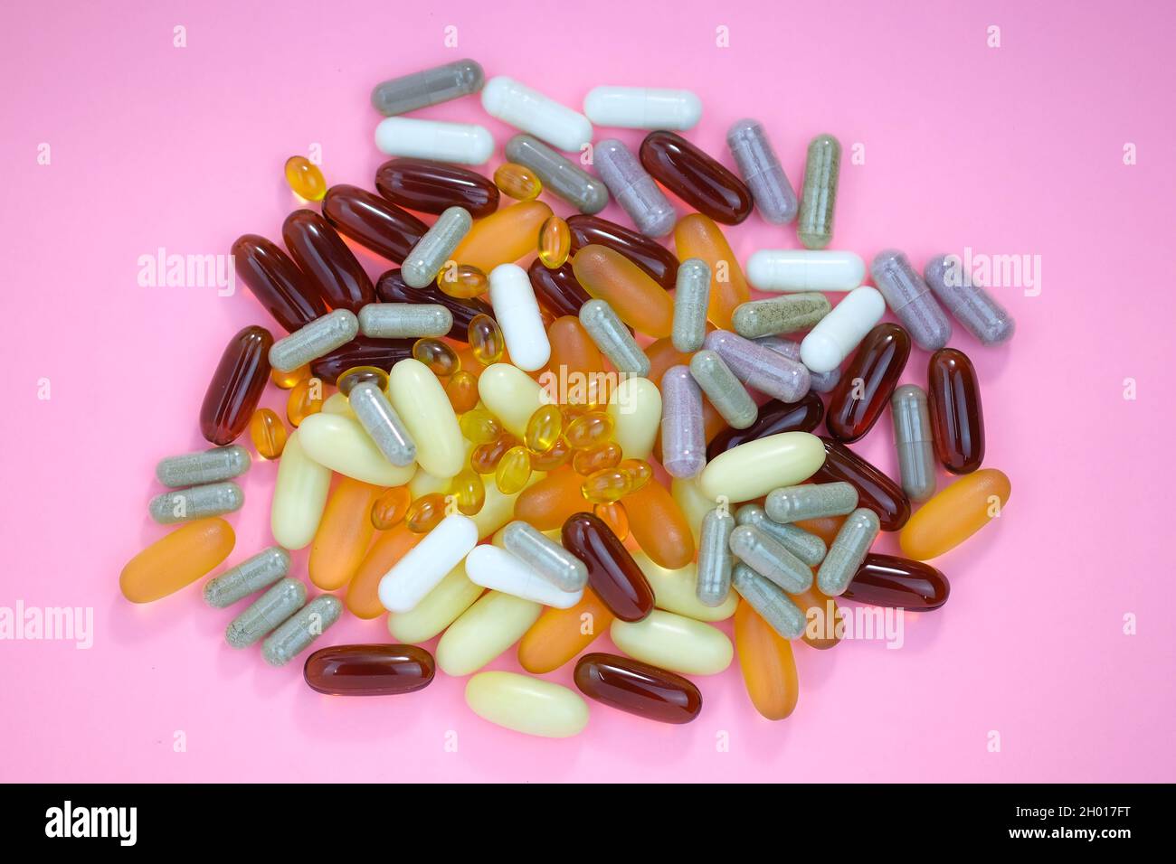 Many different capsules on a pink background top view. Brown, yellow ...