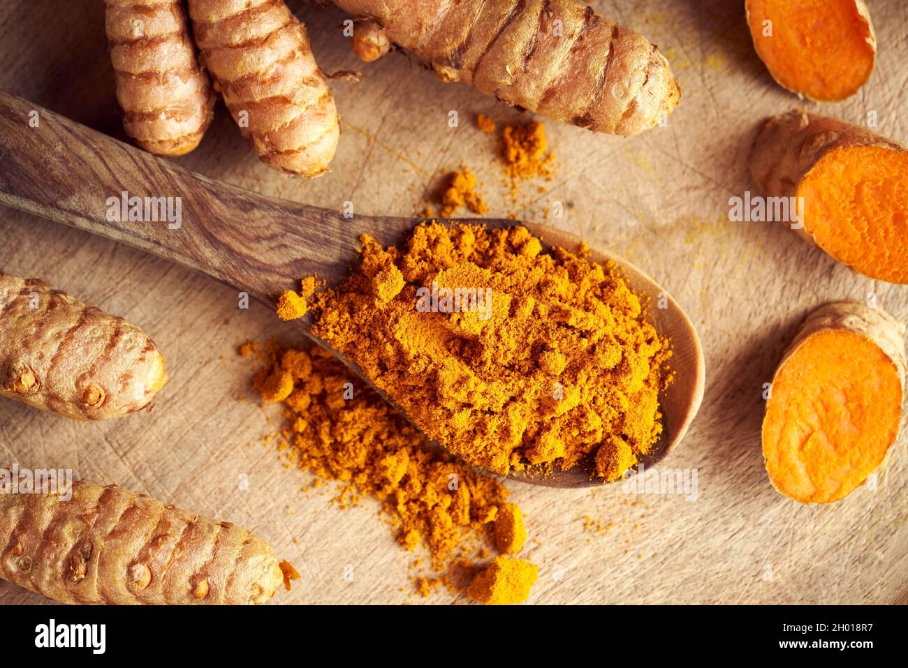 Curcuma powder on a spoon with fresh whole and cut up turmeric root ...