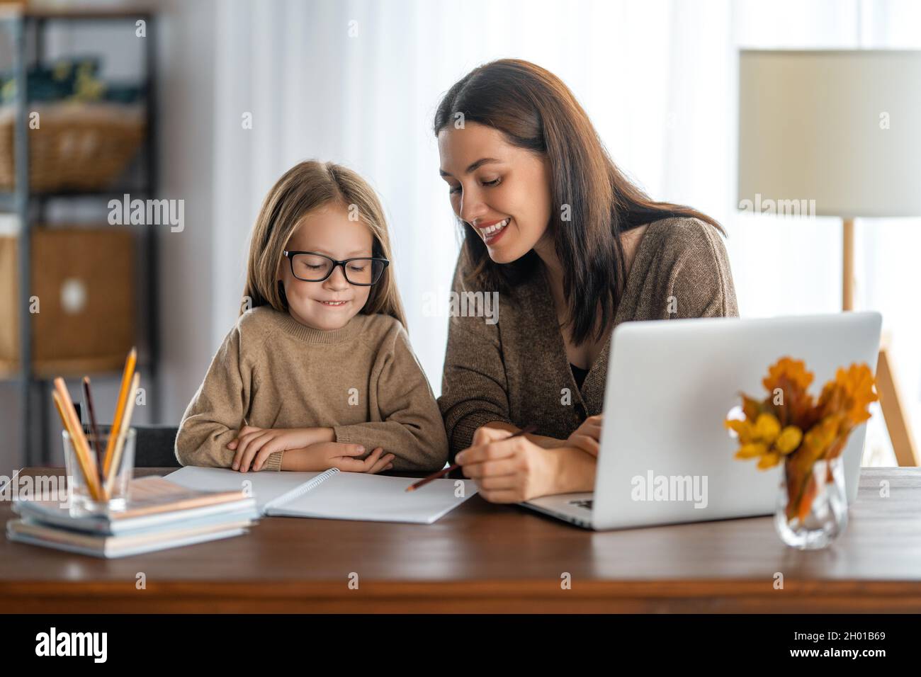 Back to school. Happy child and adult are sitting at desk. Girl doing ...