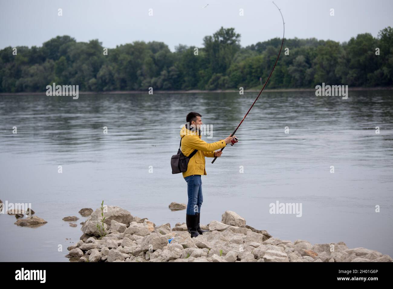 Handsome angler fishing on river coast with stone in spring time Stock ...