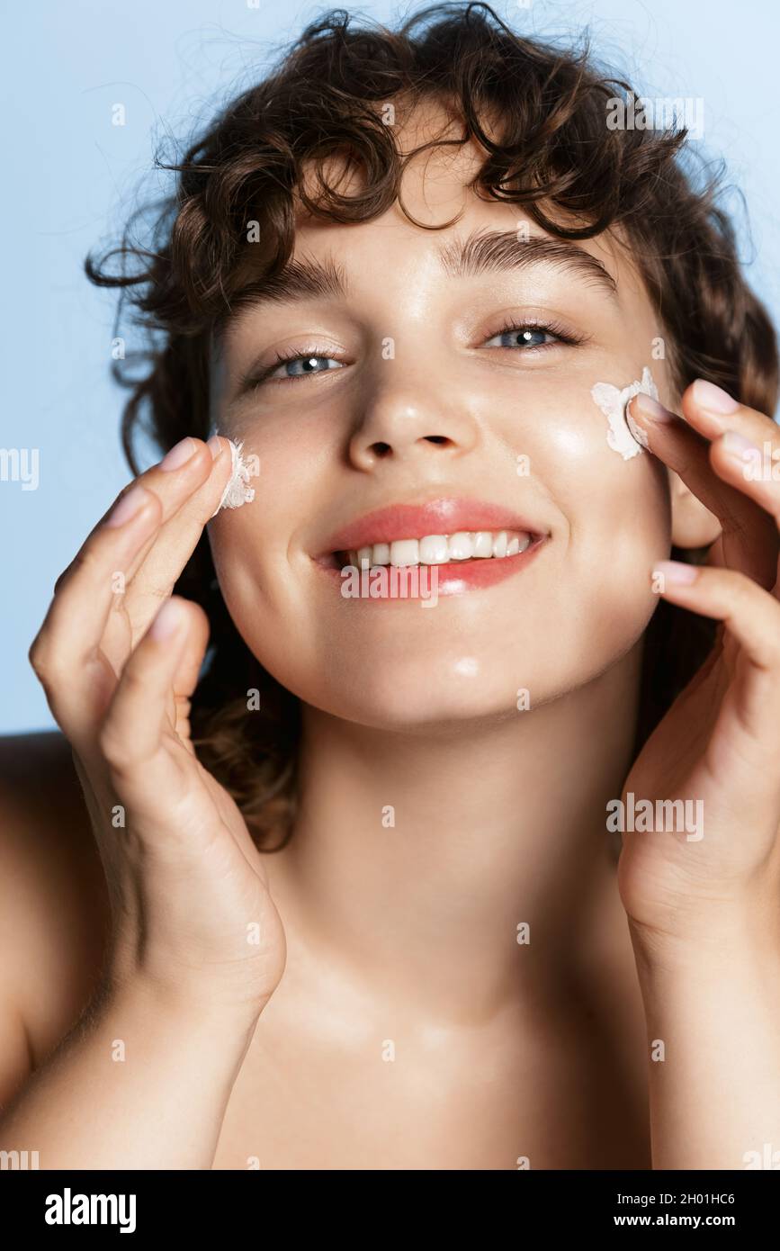 Vertical portrait of girl model apply facial cream, cleaning face with ...