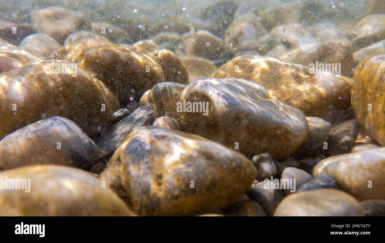 Pebbles stone underwater below water surface near lake shore, natural ...