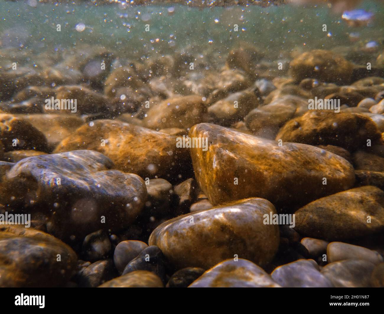 Pebbles stone underwater below water surface near lake shore, natural ...