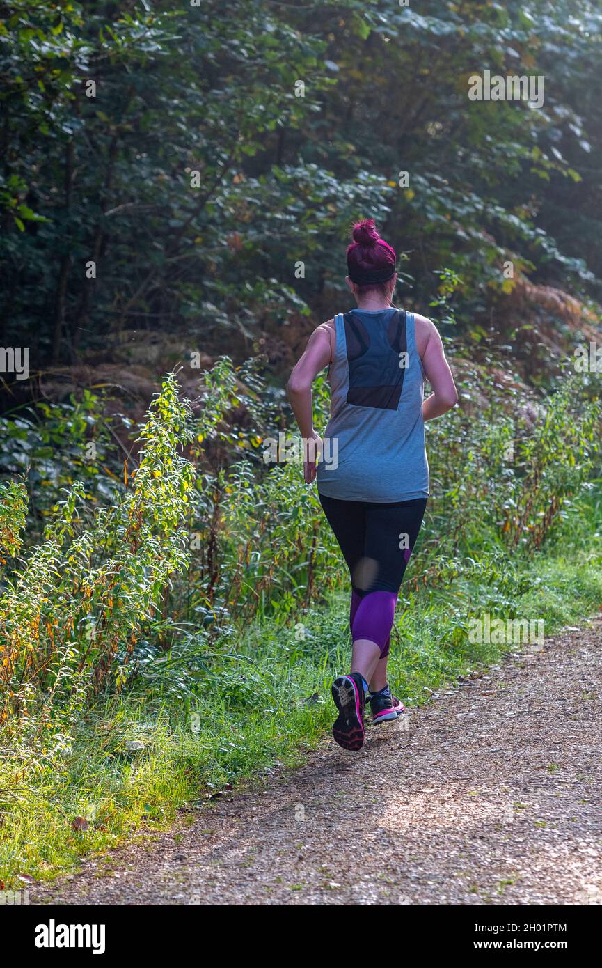 young woman running through woodland or forest wearing running gear ...