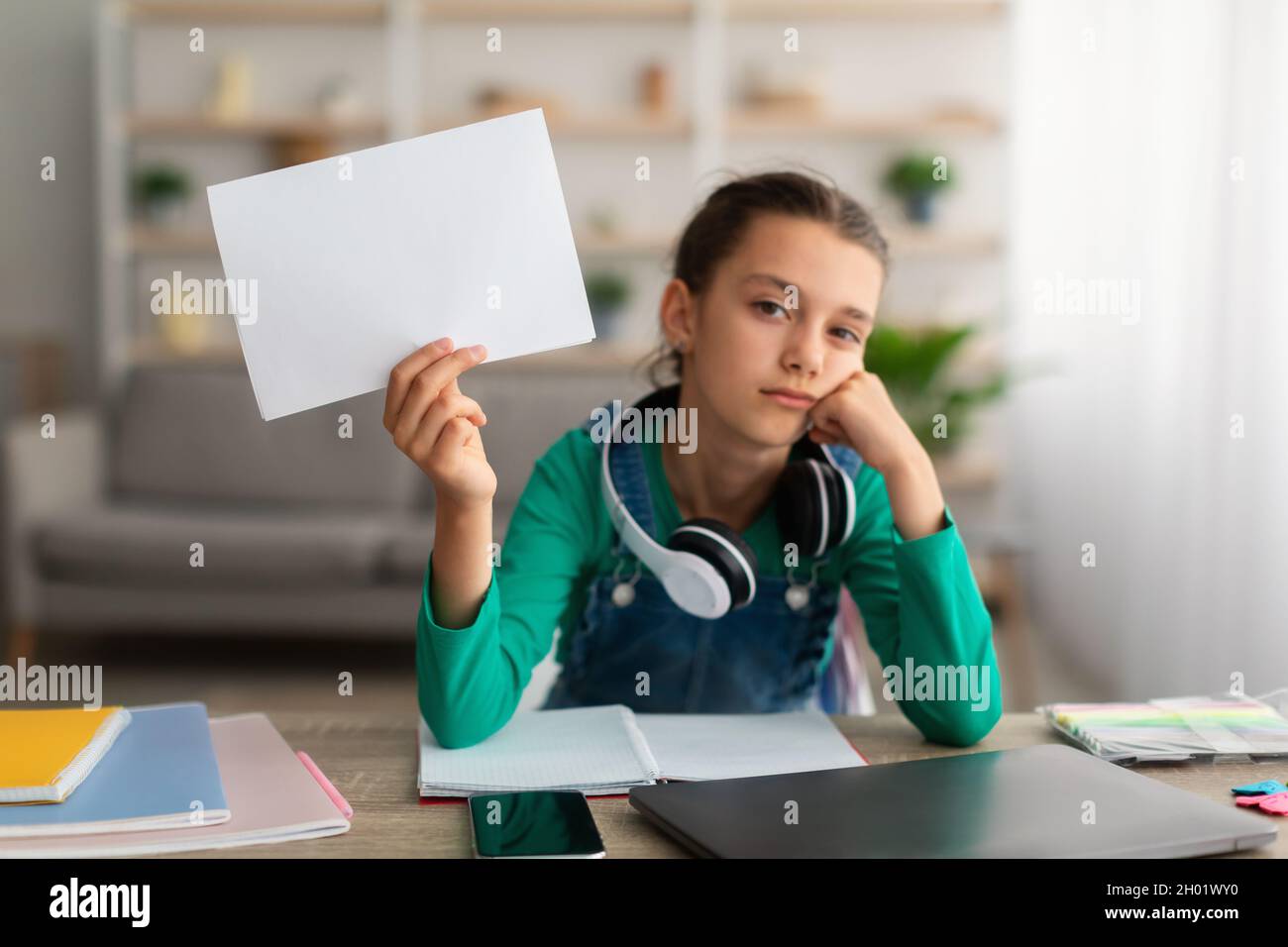 Portrait of bored teenage girl sitting at table, resting head on hand ...