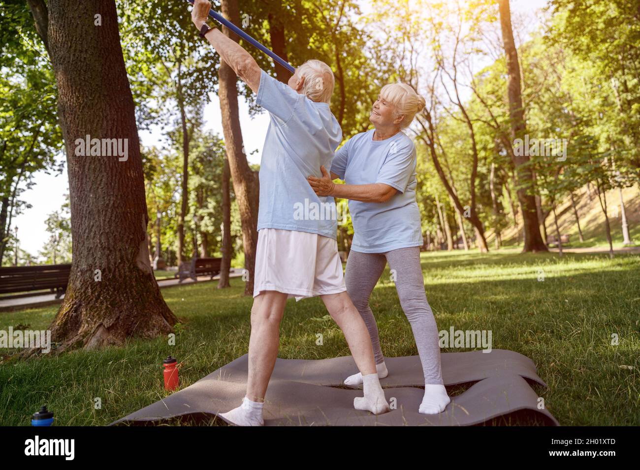 Positive mature woman supports back of senior man doing exercises with ...