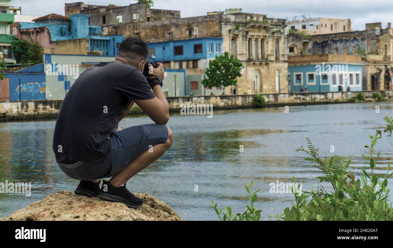 A young man from Cuba taking a photo of the waterfront buildings with a ...
