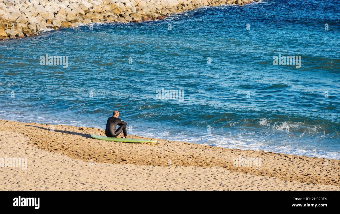 lonely surfer on the beach looking at the blue waters of the ...