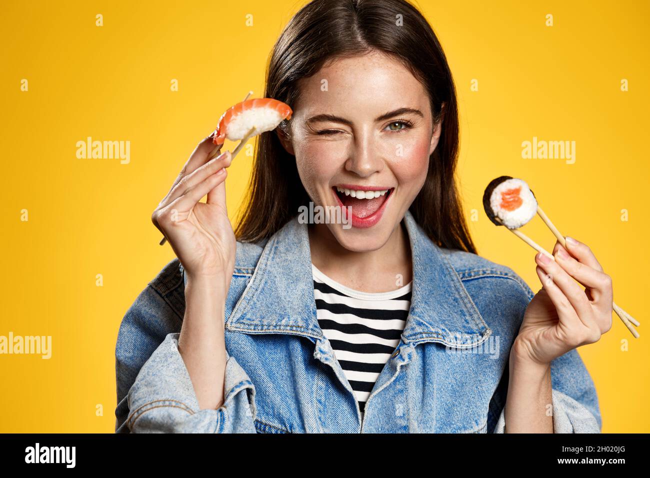 Happy smiling girl eating sushi rolls with chopsticks, holding sashimi ...