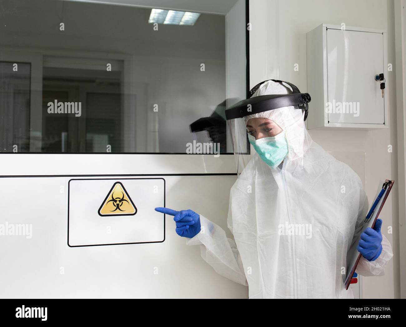 Woman in protective suit and safety mask showing biohazard sign in ...