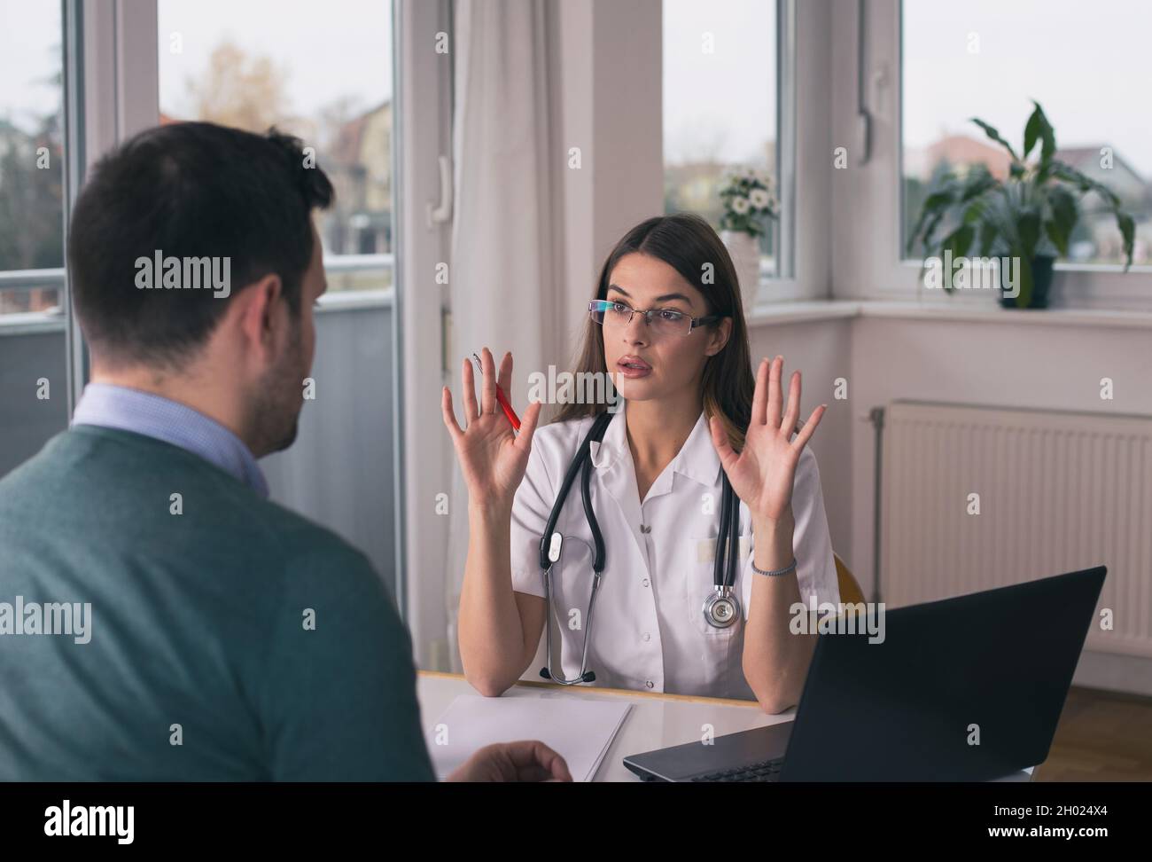 Young female doctor explaining something to a patient at desk in clinic ...