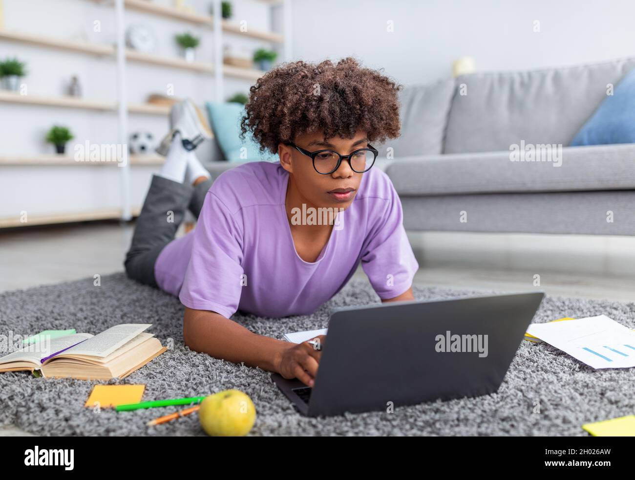 Focused black teenager using laptop pc for remote education, lying on ...