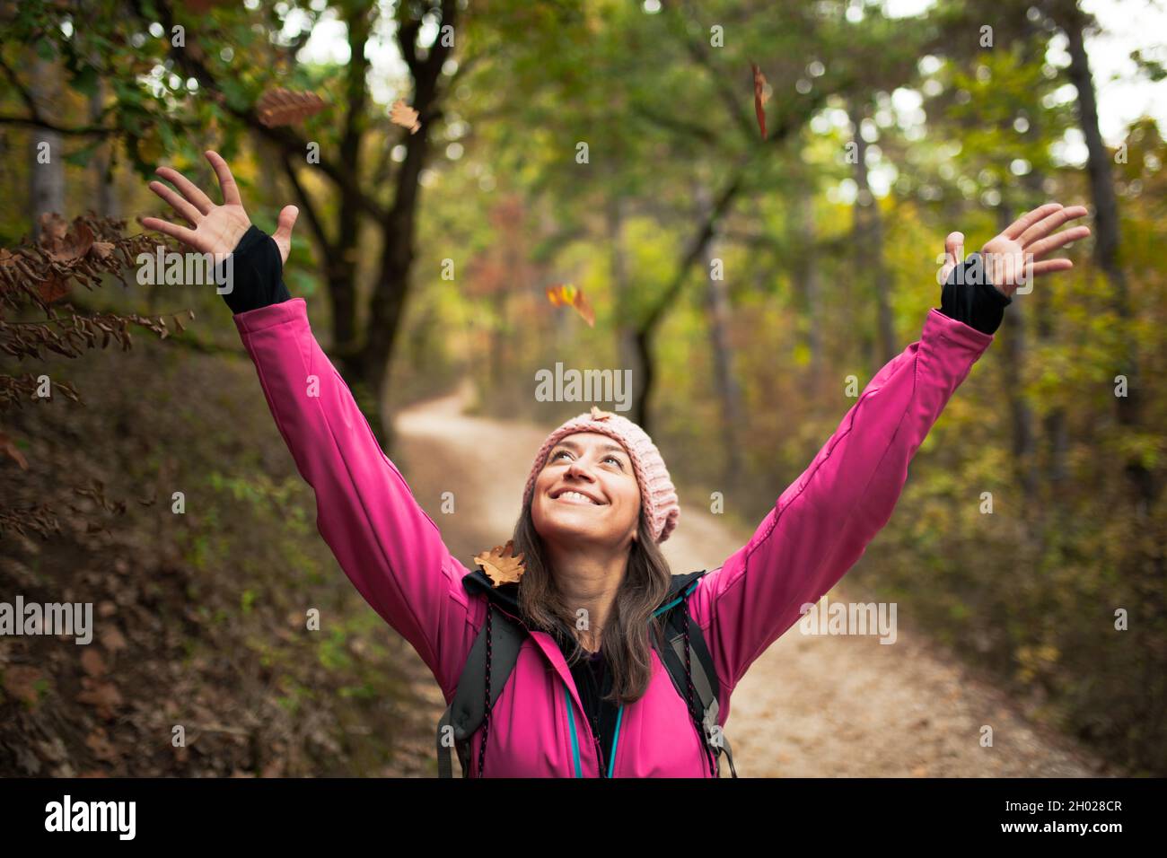 Hiking girl in pink on a trail in the forest. Hands up enjoying the ...