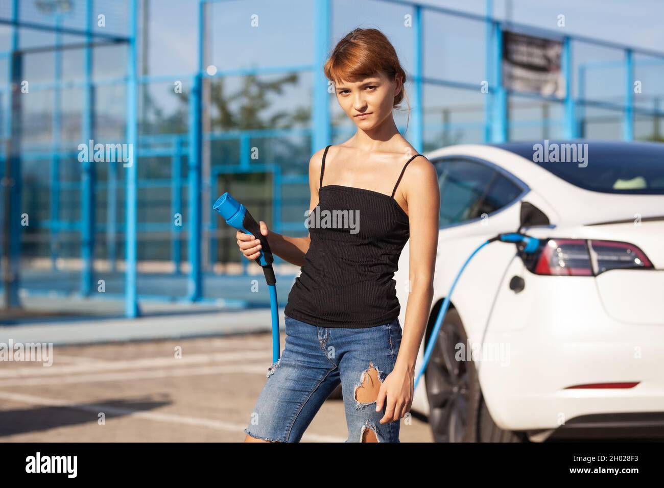 Beautiful young girl next to an electric car. Posing and holding a ...
