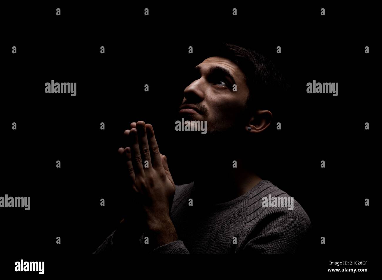 Headshot of serious confident young man praying in dark room. Lit from ...