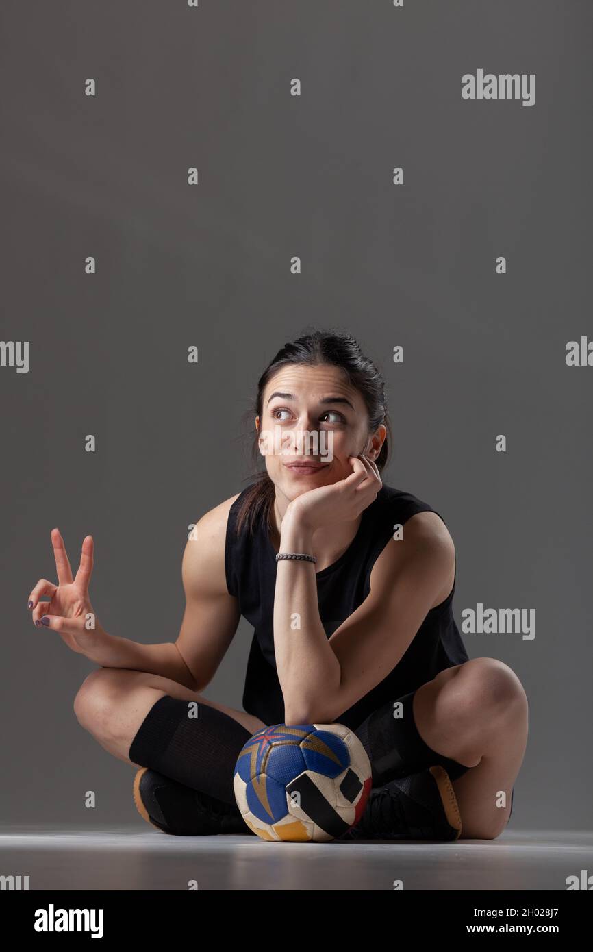 Handball player sitting on the ground. Girl posing with ball and making ...