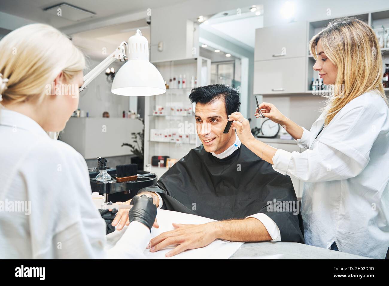 Two female beauticians taking care of man hair and nails Stock Photo ...