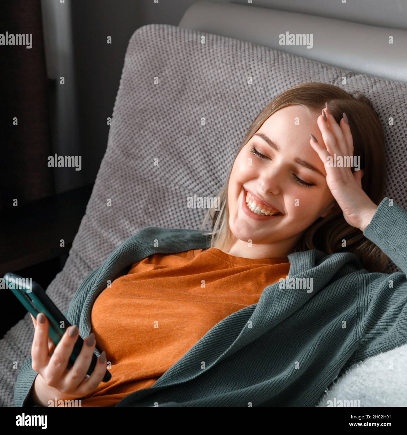 Woman Laughs Looking Into Smartphone Lying On The Couch Teenage Girl