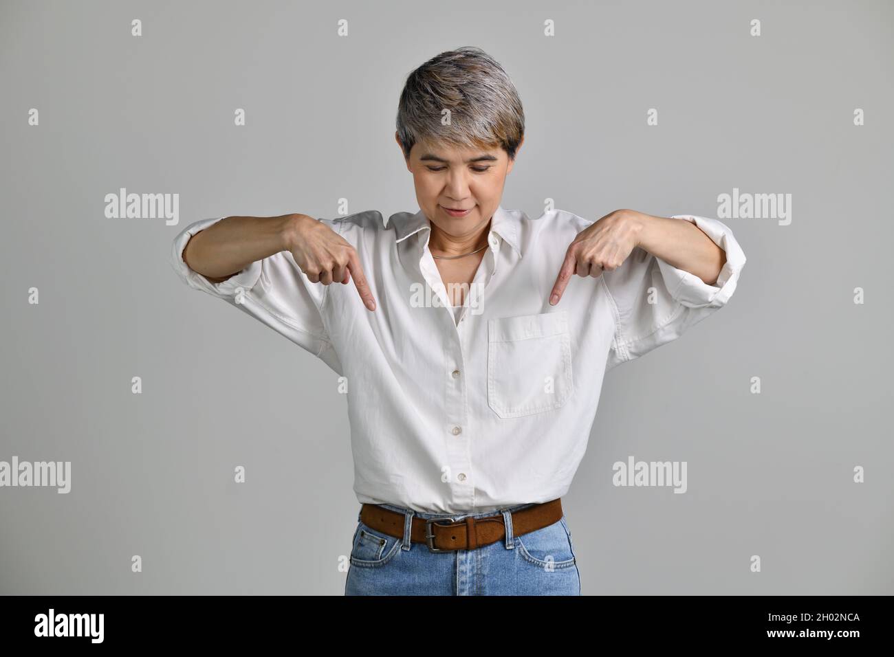 Middle aged Asian woman pointing fingers down at empty copy space for ...