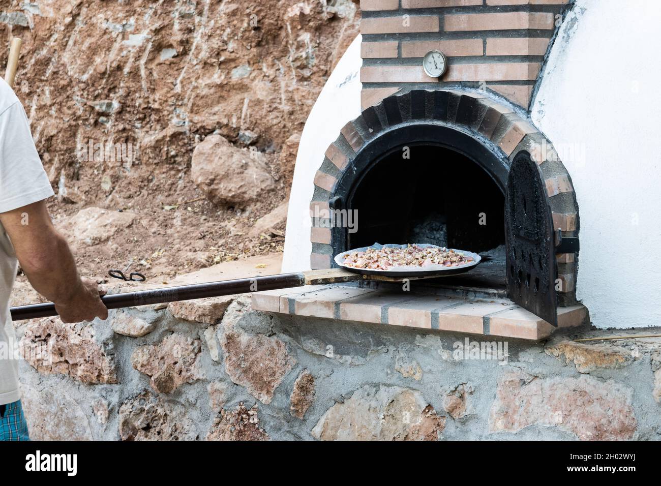 Man putting pizza in handmade white painted wood oven built outdoors ...