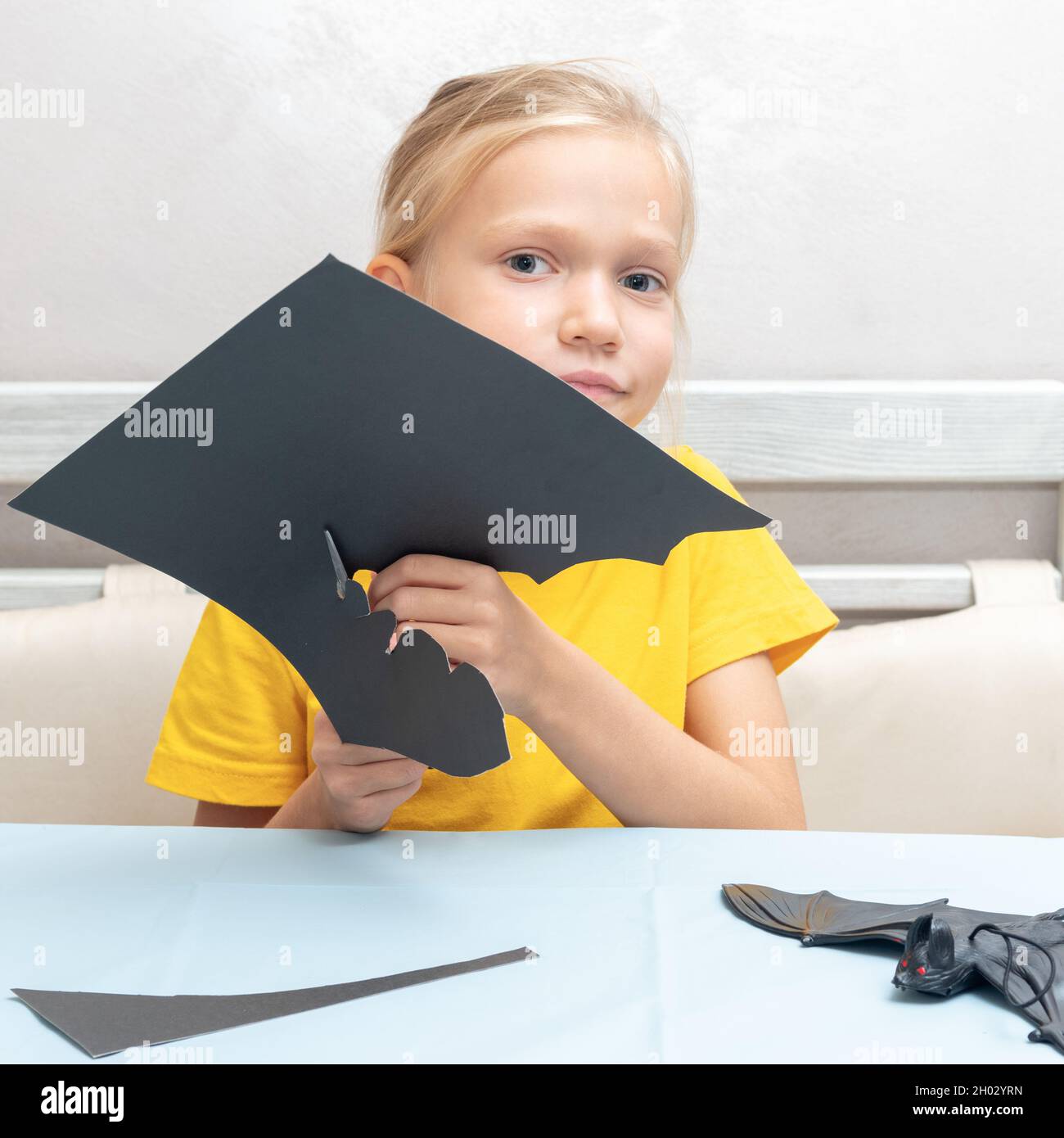 A girl cuts a Halloween decoration at home from black paper. DIY craft ...