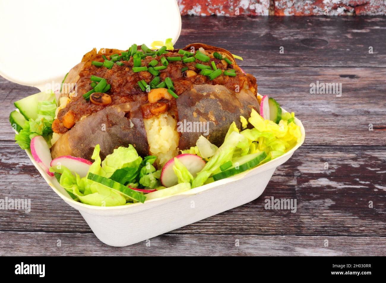Chilli beef filled baked jacket potato with fresh salad in a take away ...