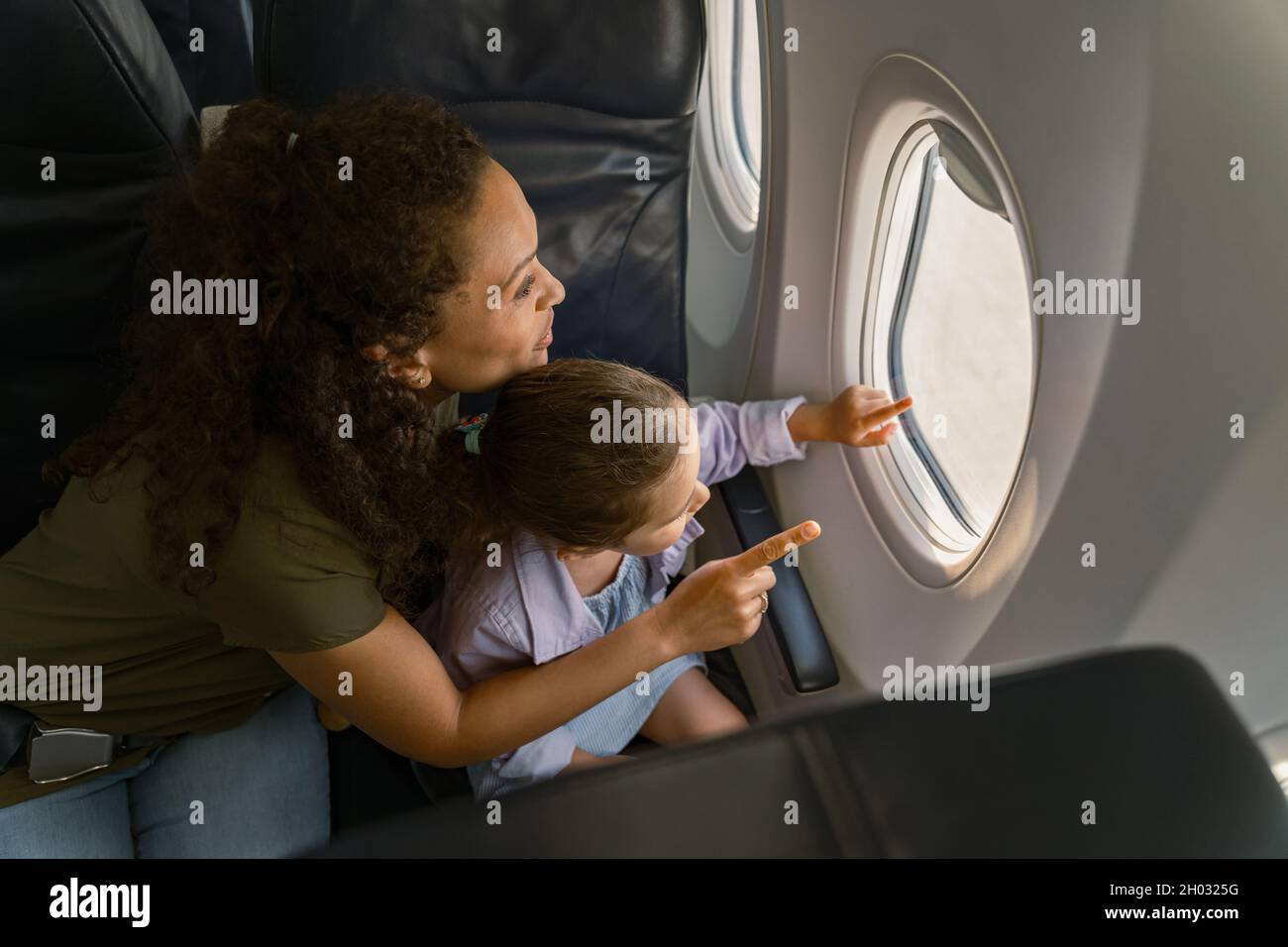 Happy mother and her daughter looking at the scenery outside the plane ...
