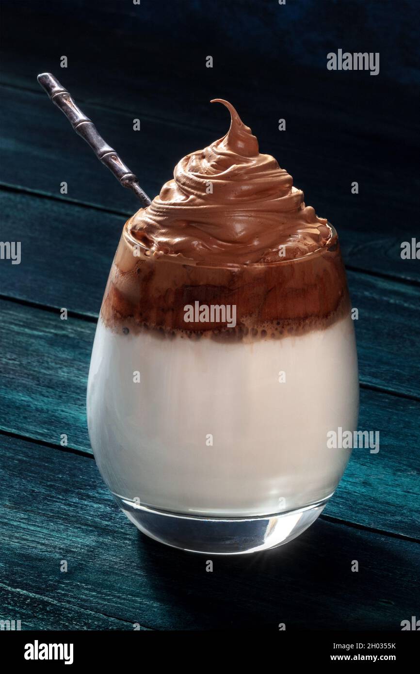 Dalgona cold coffee with a spoon, on a dark blue background. Korean ...