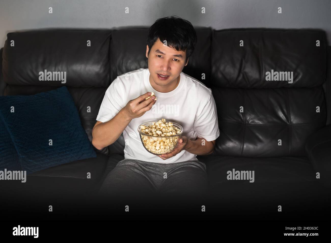 young man watching TV and eating popcorn on sofa at night Stock Photo ...