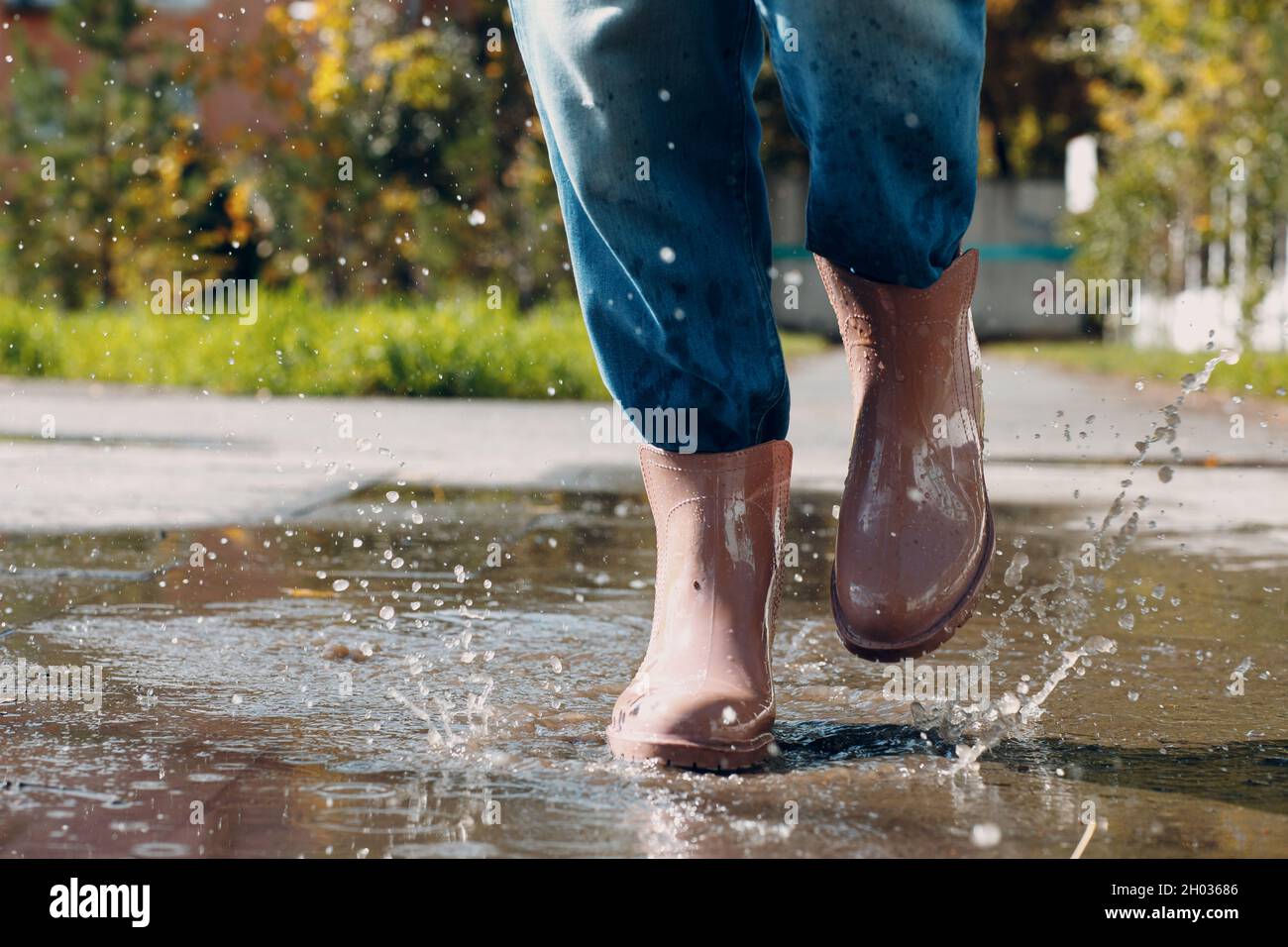Woman wearing rain rubber boots walking running and jumping into puddle with water splash and ...