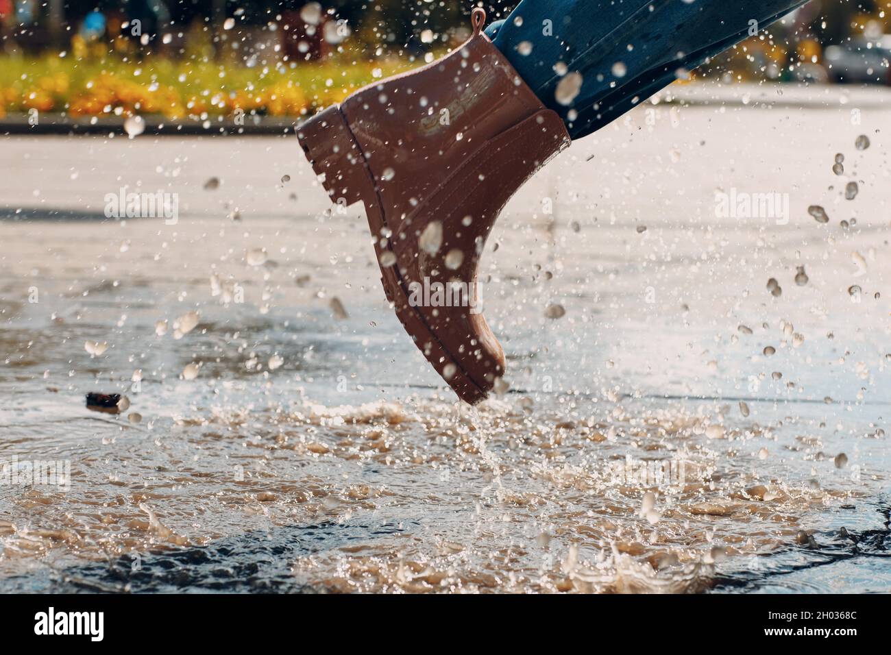 Woman wearing rain rubber boots walking running and jumping into puddle with water splash and ...
