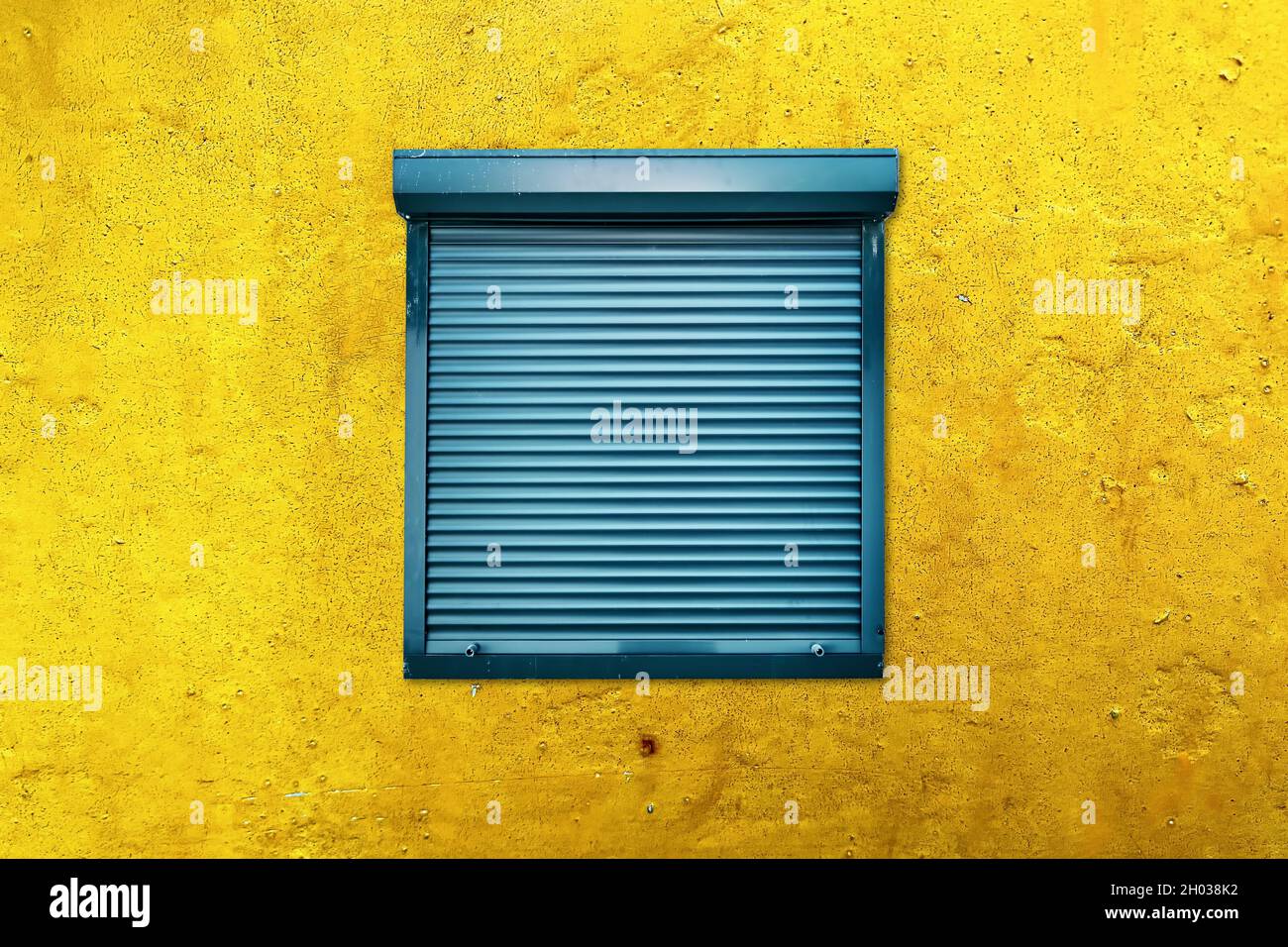 Square window with closed blue blinds or rolling shutter on a yellow ...