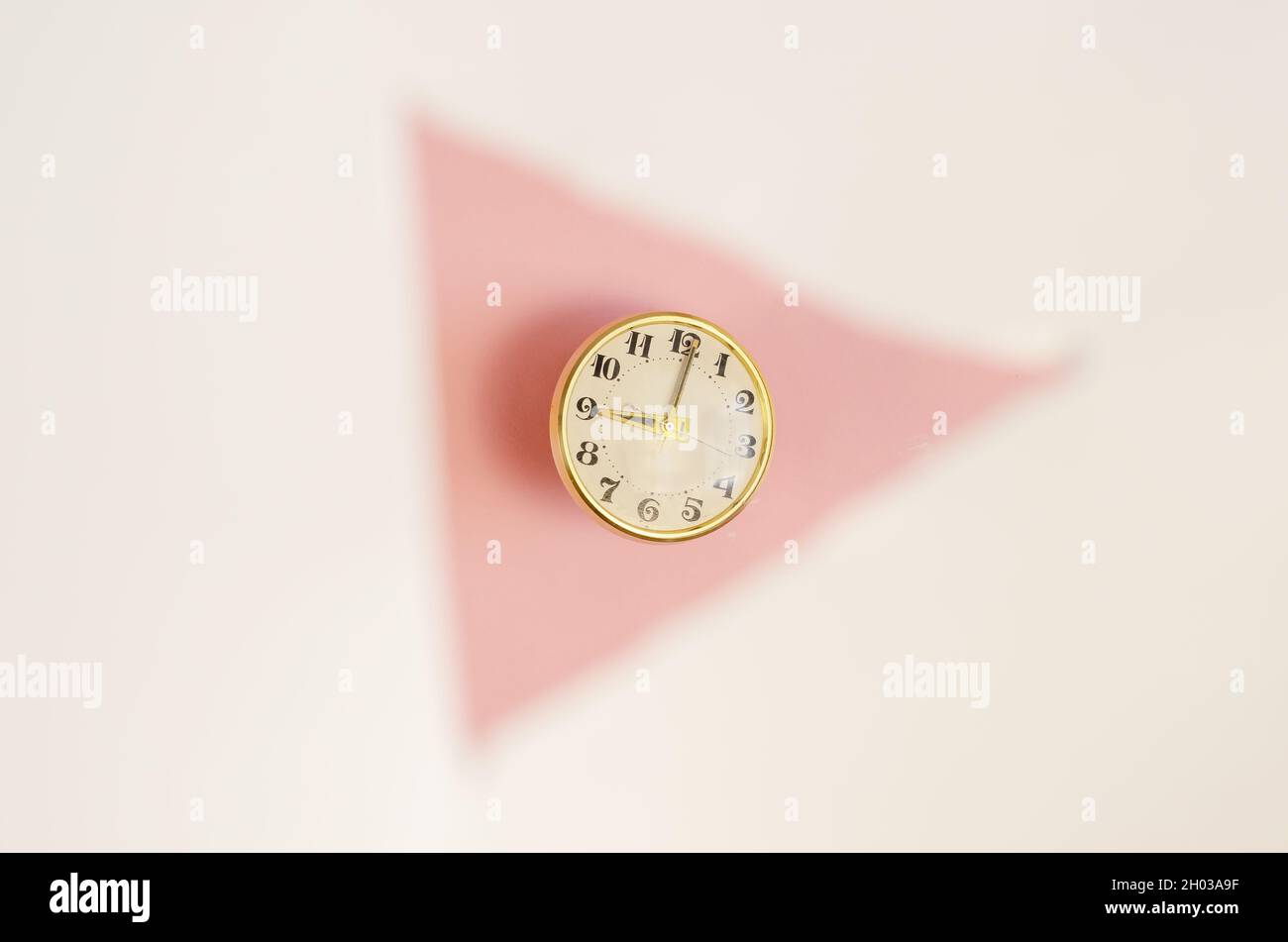 Vintage clock in a blurred white triangle on a pink background. Round ...