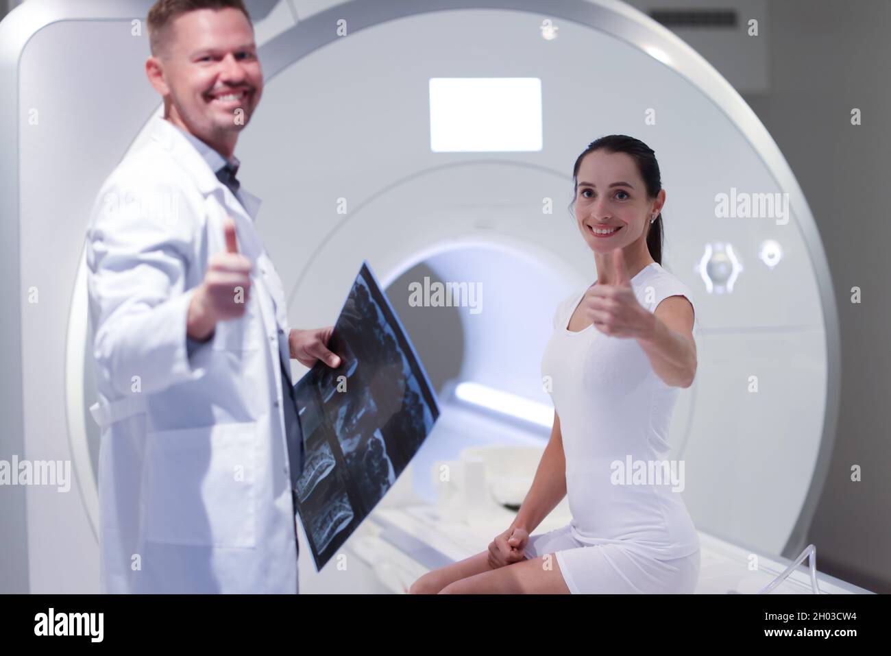 Smiling male doctor and female patient hold thumbs up in office for MRI ...