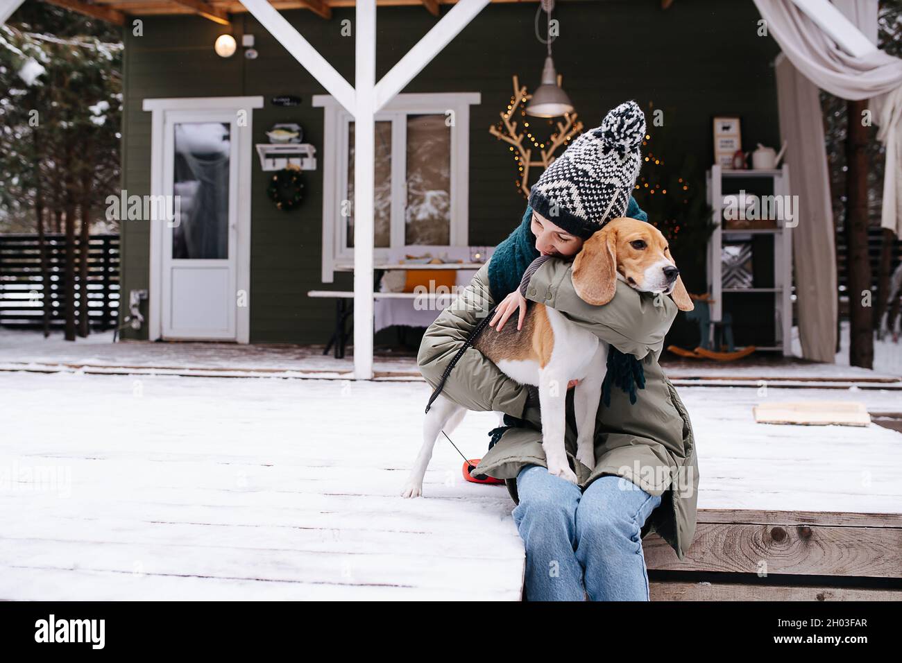 Gentle woman sitting on a snowy terrace in front of the house, hugging ...