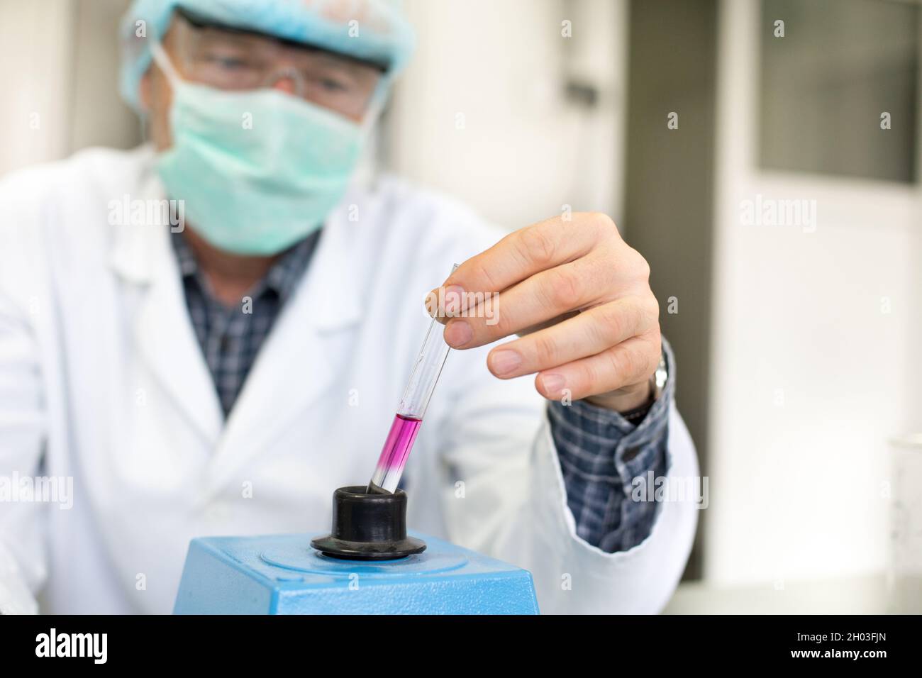 Close up of researcher's hand holding test tube with fluid above ...