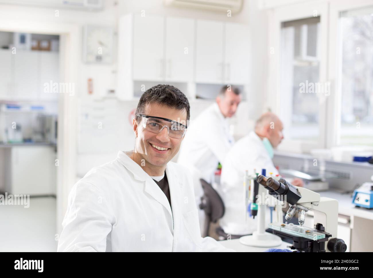 Portrait of smiling handsome biologist sitting beside microscope with ...
